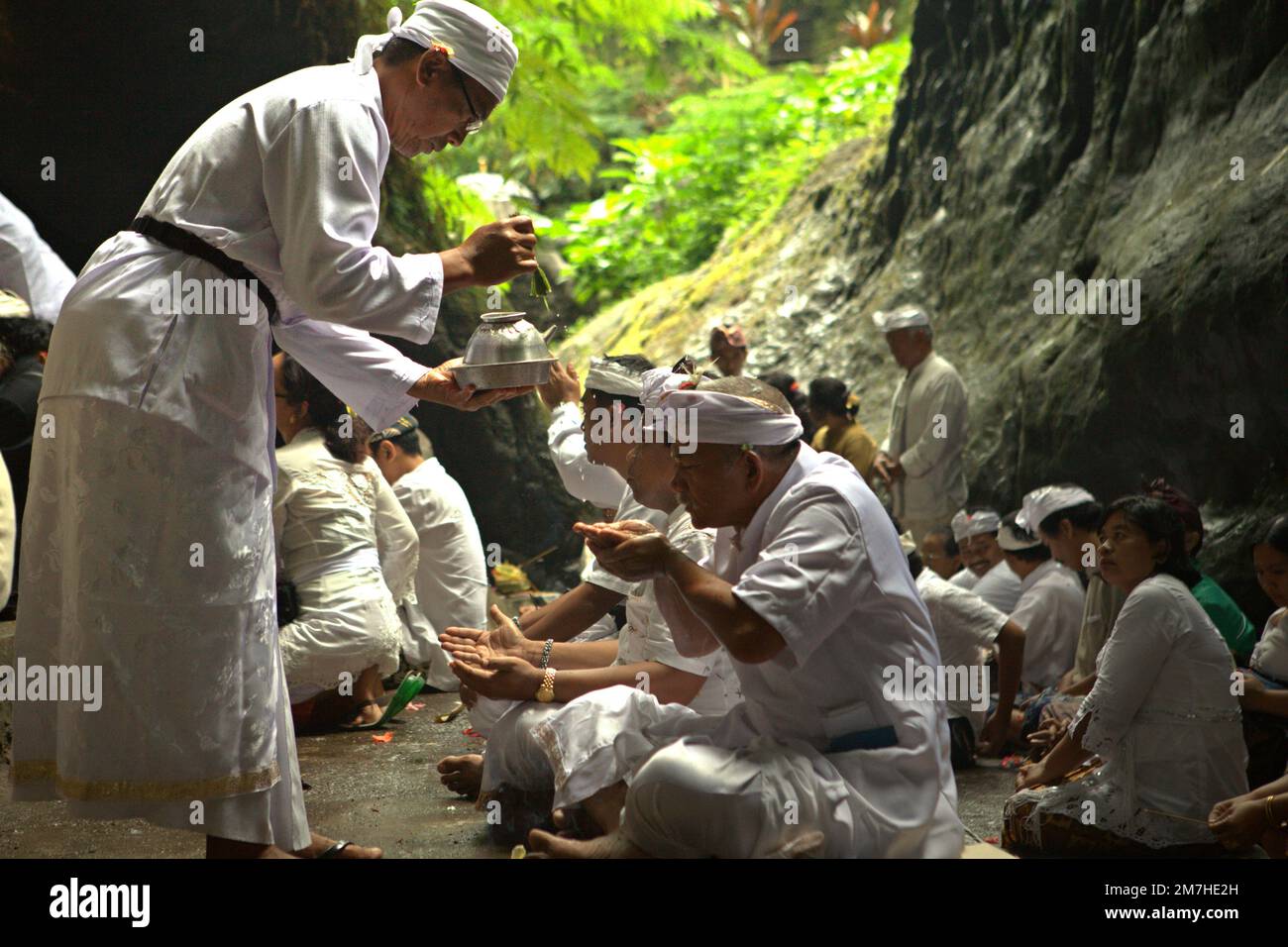 A Balinese Hindu priest is splashing people with water during a ritual ...