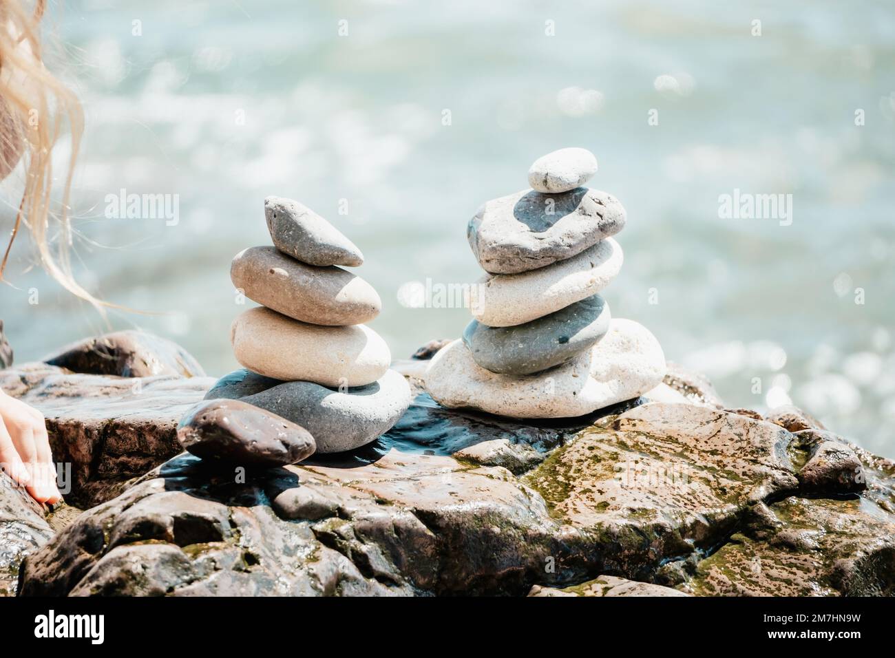 Woman with daughter bilds stones pyramid on seashore on a sunny day on ...