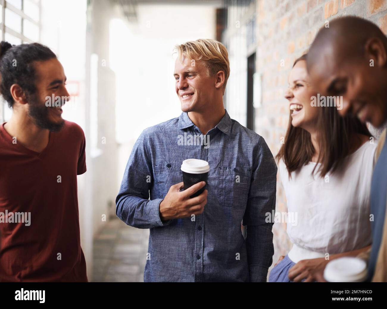 Sharing a moment with friends. four young adults standing in a corridor ...