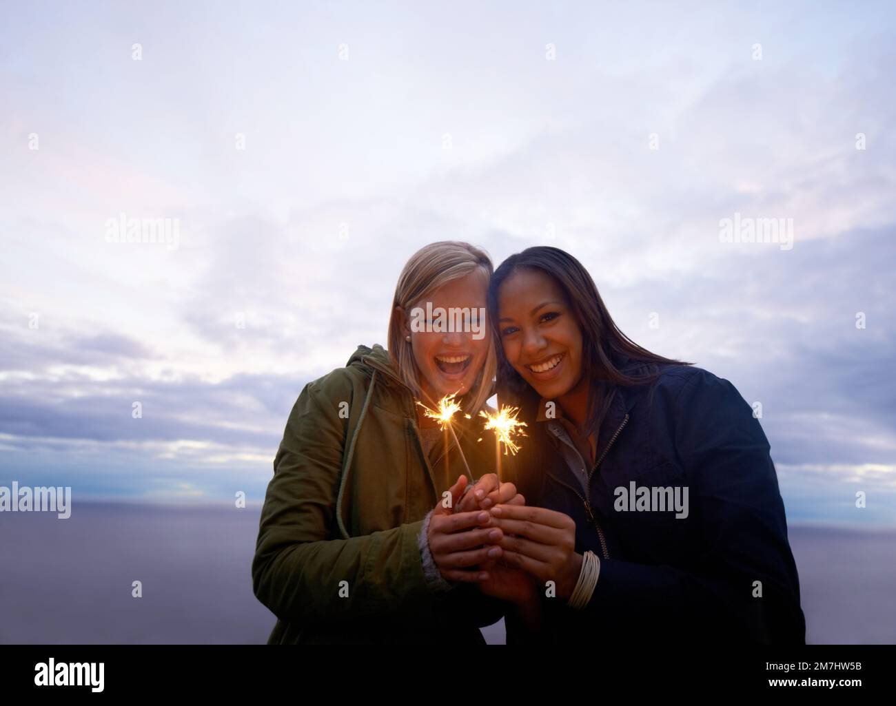 They burn so fast. Two young women holding sparklers with the ocean and ...