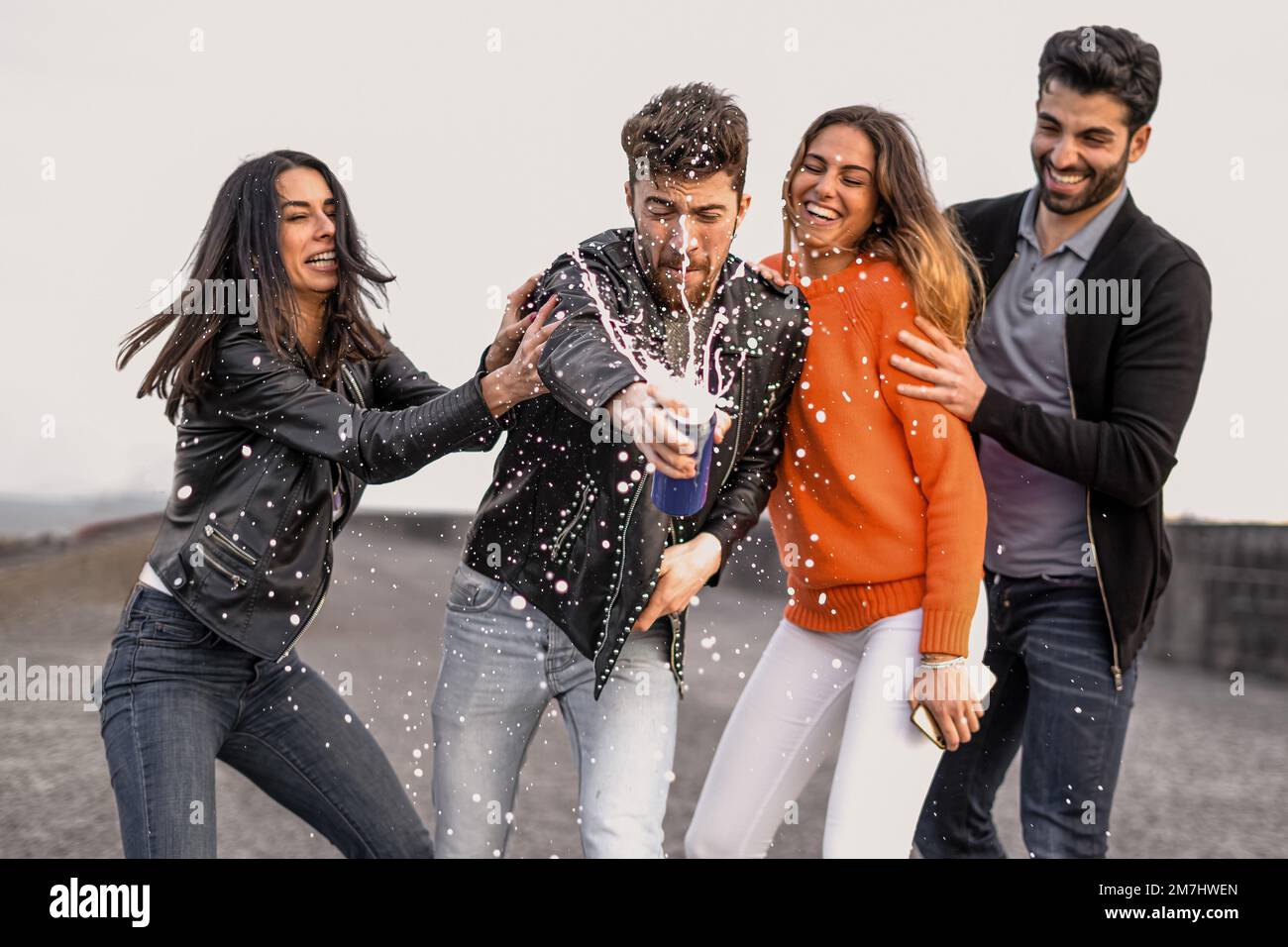 An excited group of friends have fun opening a can of beer, making the ...