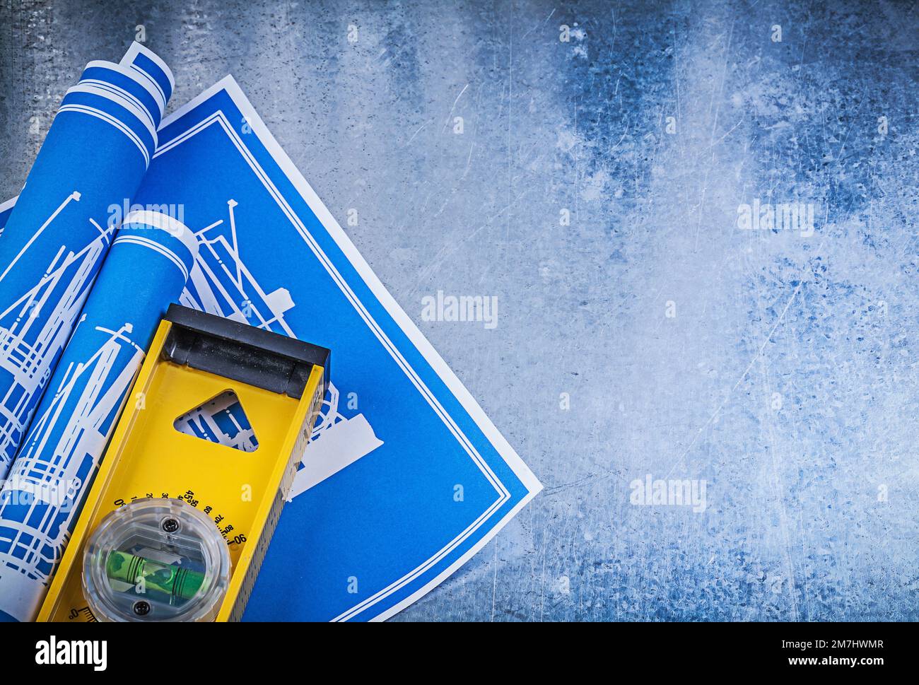 Blue rolled blueprints yellow construction level on metallic background ...