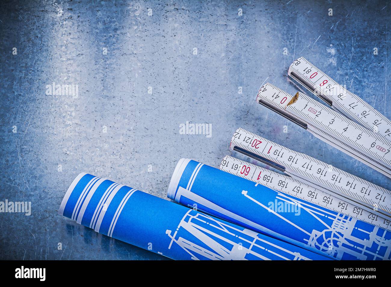Blue rolled construction drawings wooden meter on scratched metallic ...
