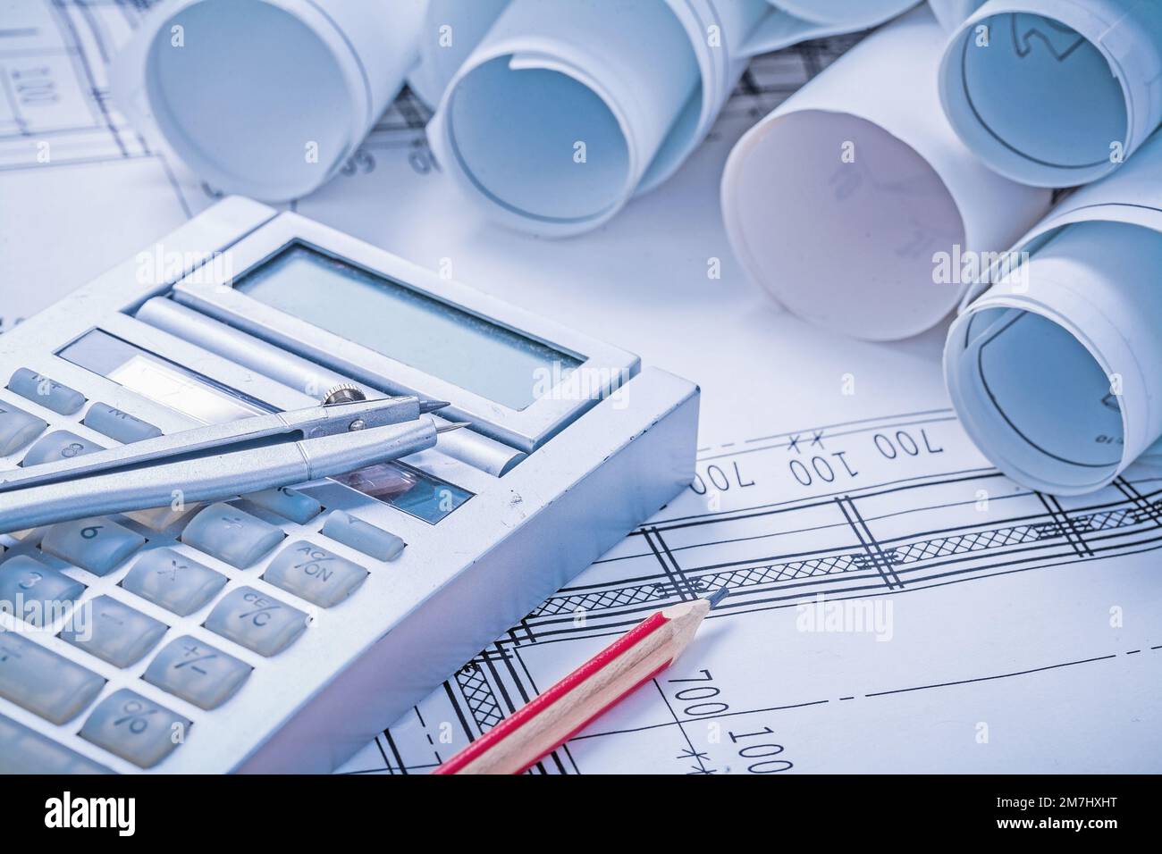 compass on calculator pencil and stack of white rolled up blueprints ...