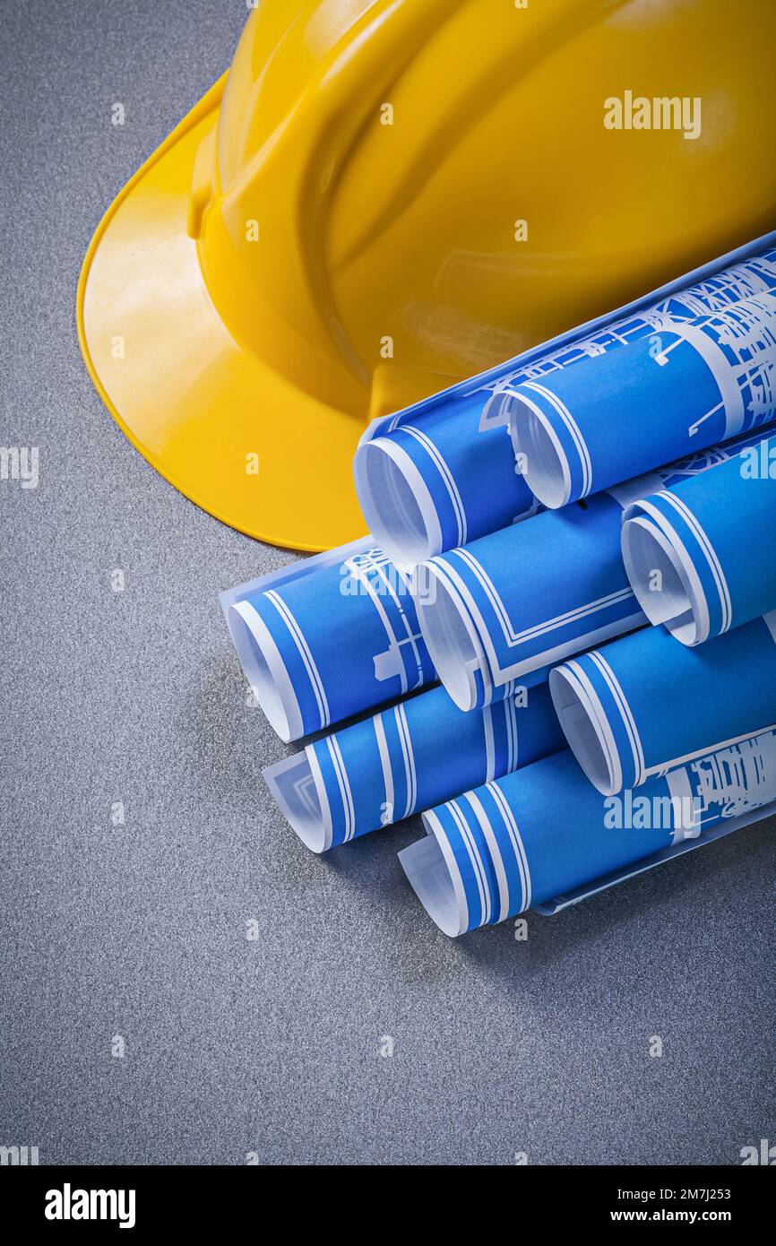 Yellow hard hat blue rolled engineering drawings on grey background ...
