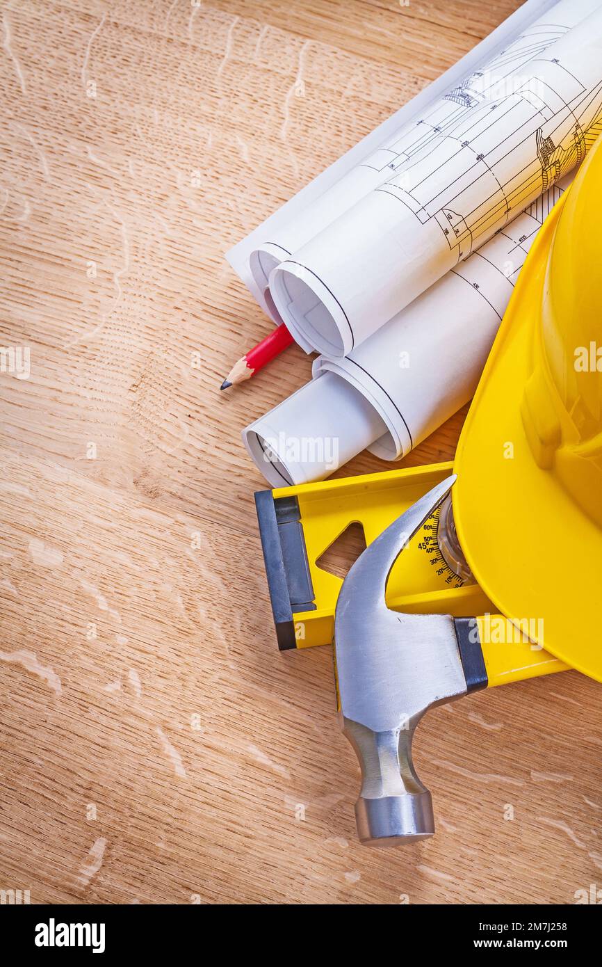 yellow helmet claw hammer level rolled blueprints pencil on wooden ...