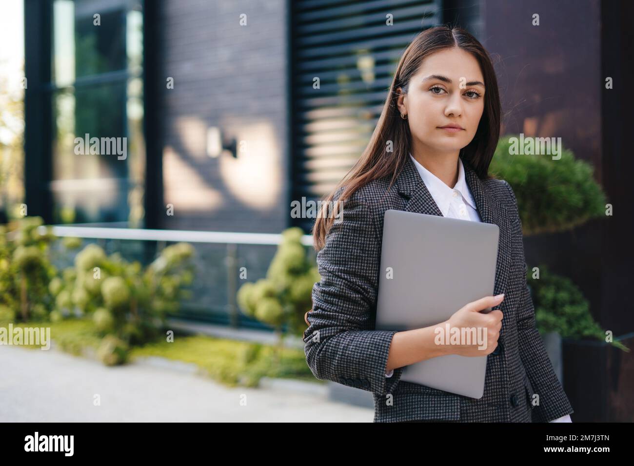 Businesswoman with laptop walking on city street looking at camera and ...