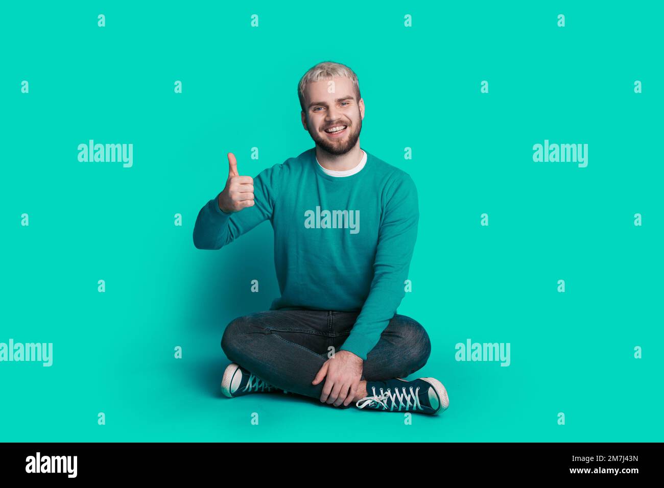 Full size photo of young man sitting on floor show thumbs-up approve ...