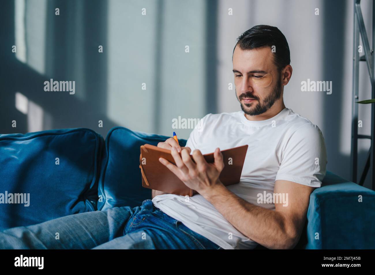 Young man sitting on couch writing down information in note book ...