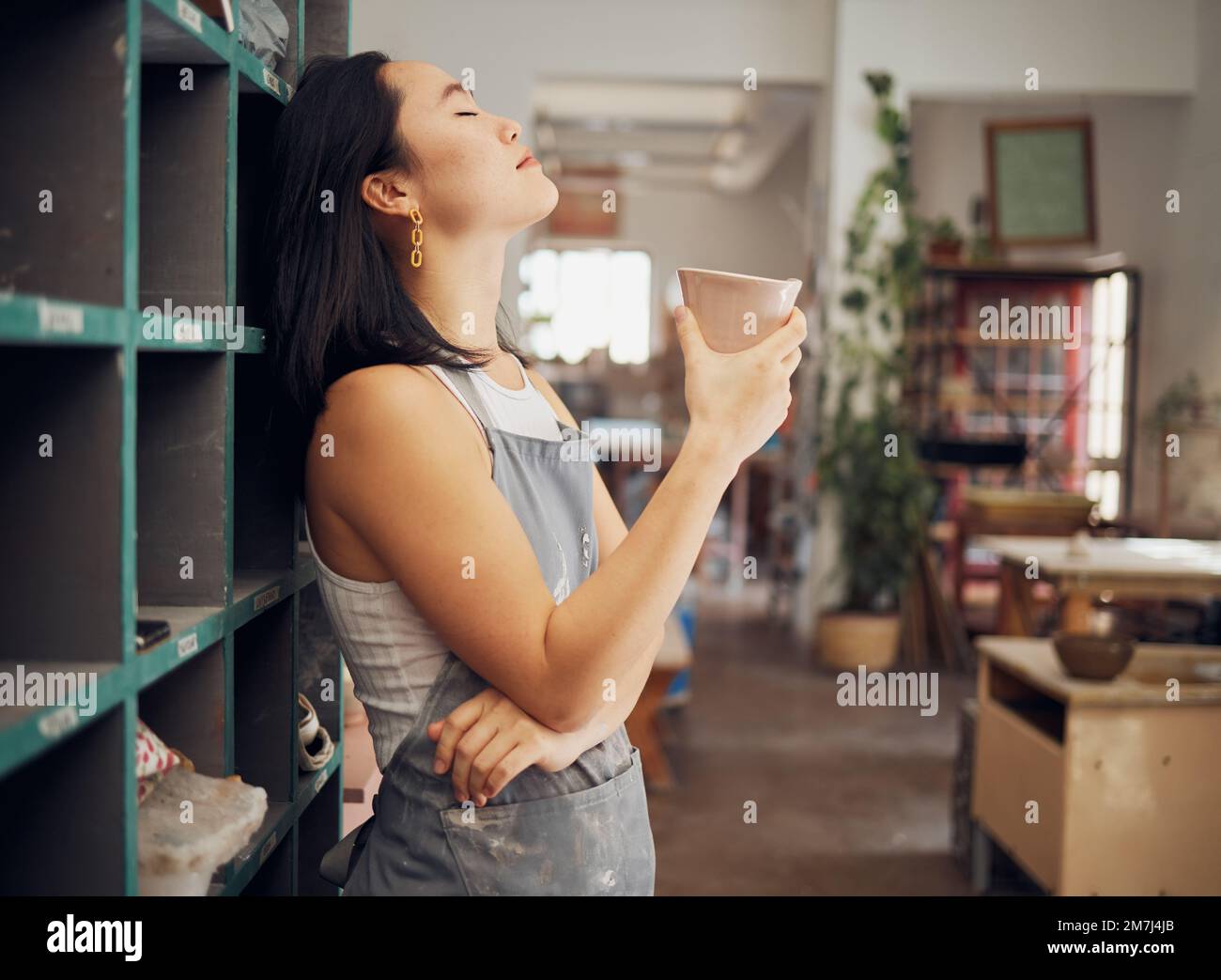 Pottery, coffee and relax with an asian woman taking a break from design in her studio or ...