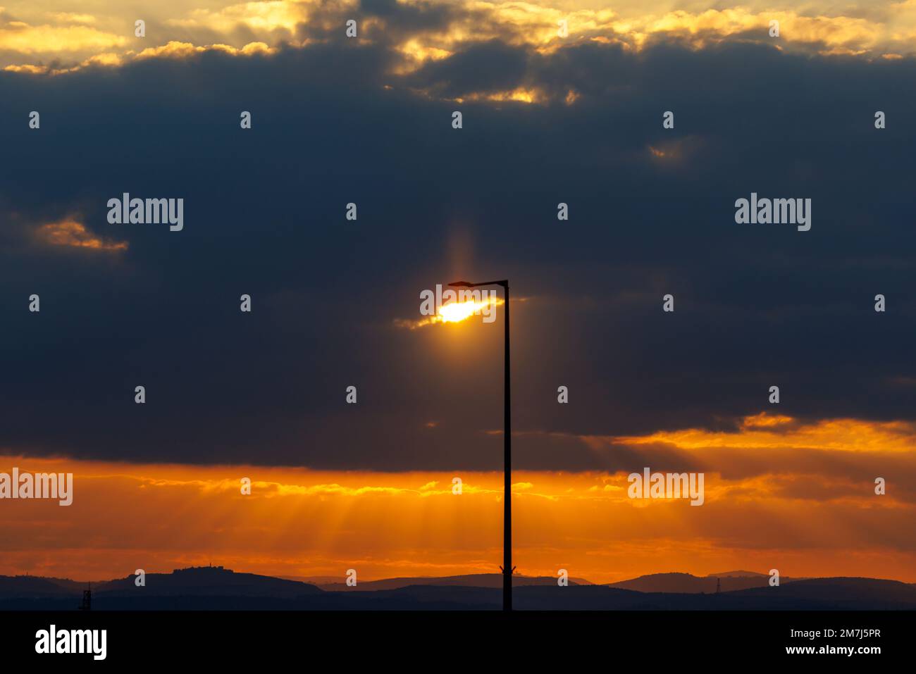 A silhouette of a light pole under a bright cloudy sunset sky Stock ...