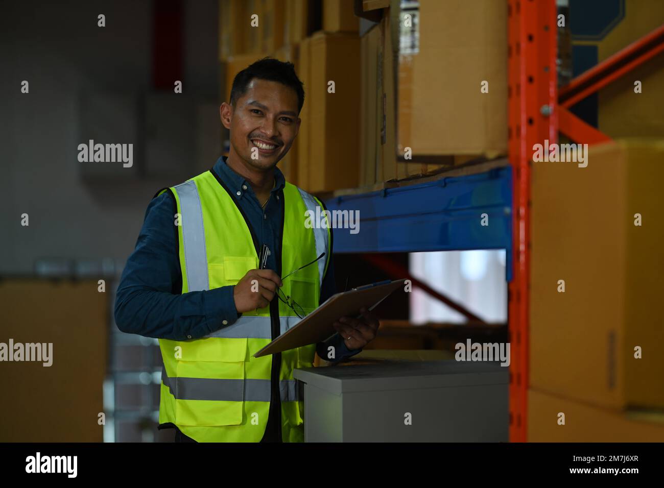Smiling asian male warehouse worker checking goods and supplies on ...