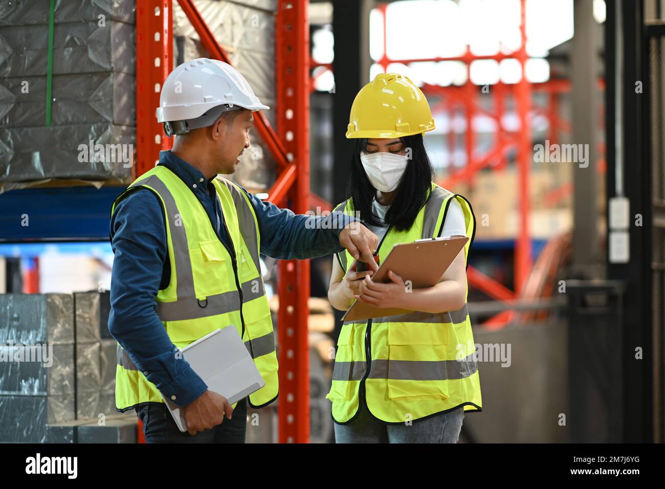 Two warehouse coworkers talking to each other while standing between ...