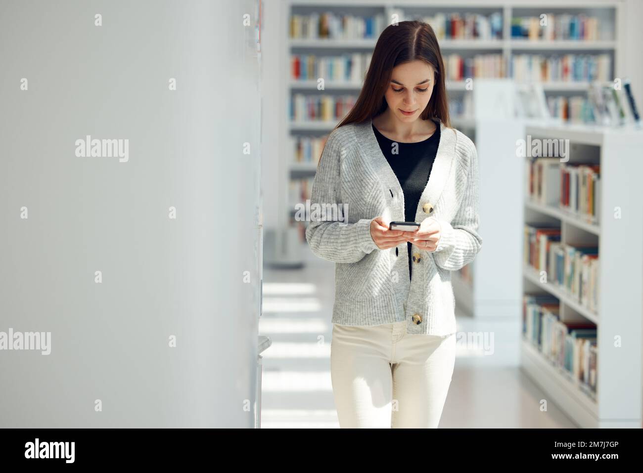 Phone, library and woman networking on social media, mobile app or the ...