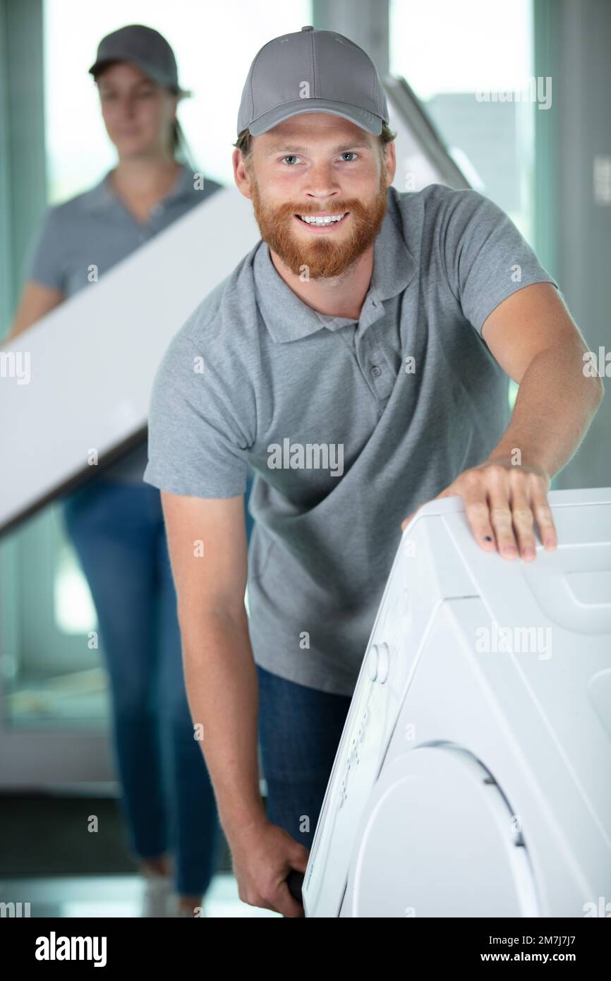 two young male professional movers in uniform delivery washing machine ...