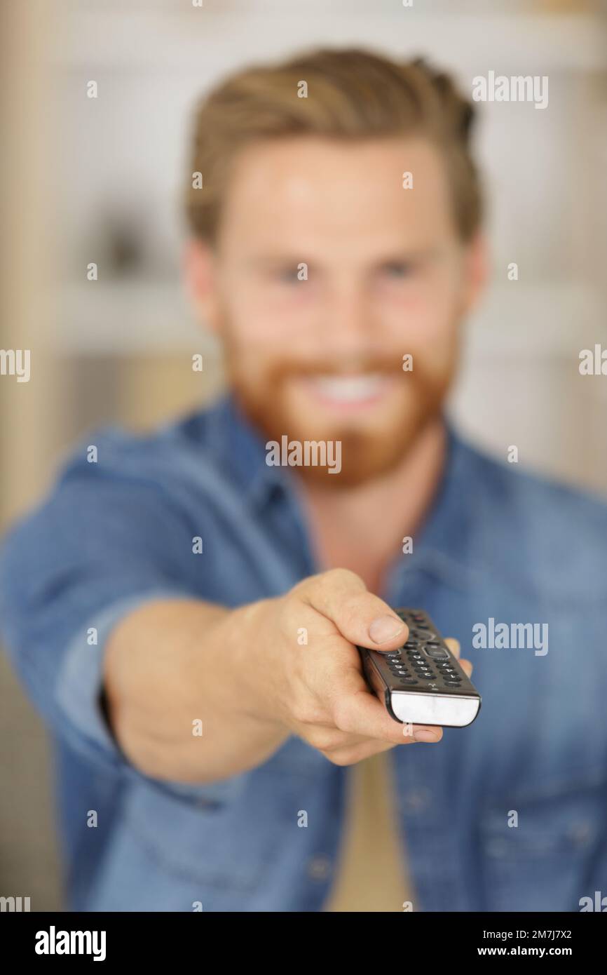 Handsome young man holding remote control and changing tv channels hi ...
