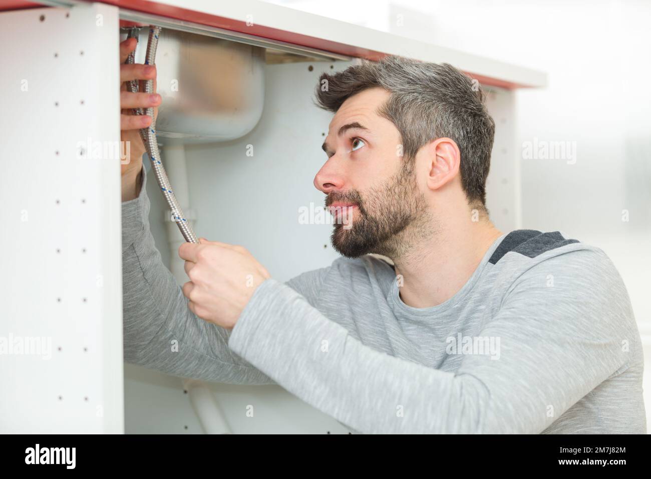 man fitting flexible pipe under kitchen sink Stock Photo - Alamy