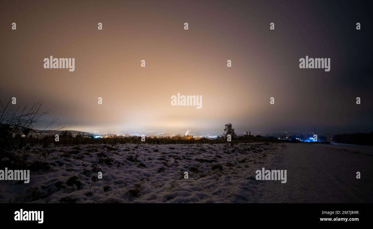 night landscape of a snowy field and a city with lights on the horizon ...