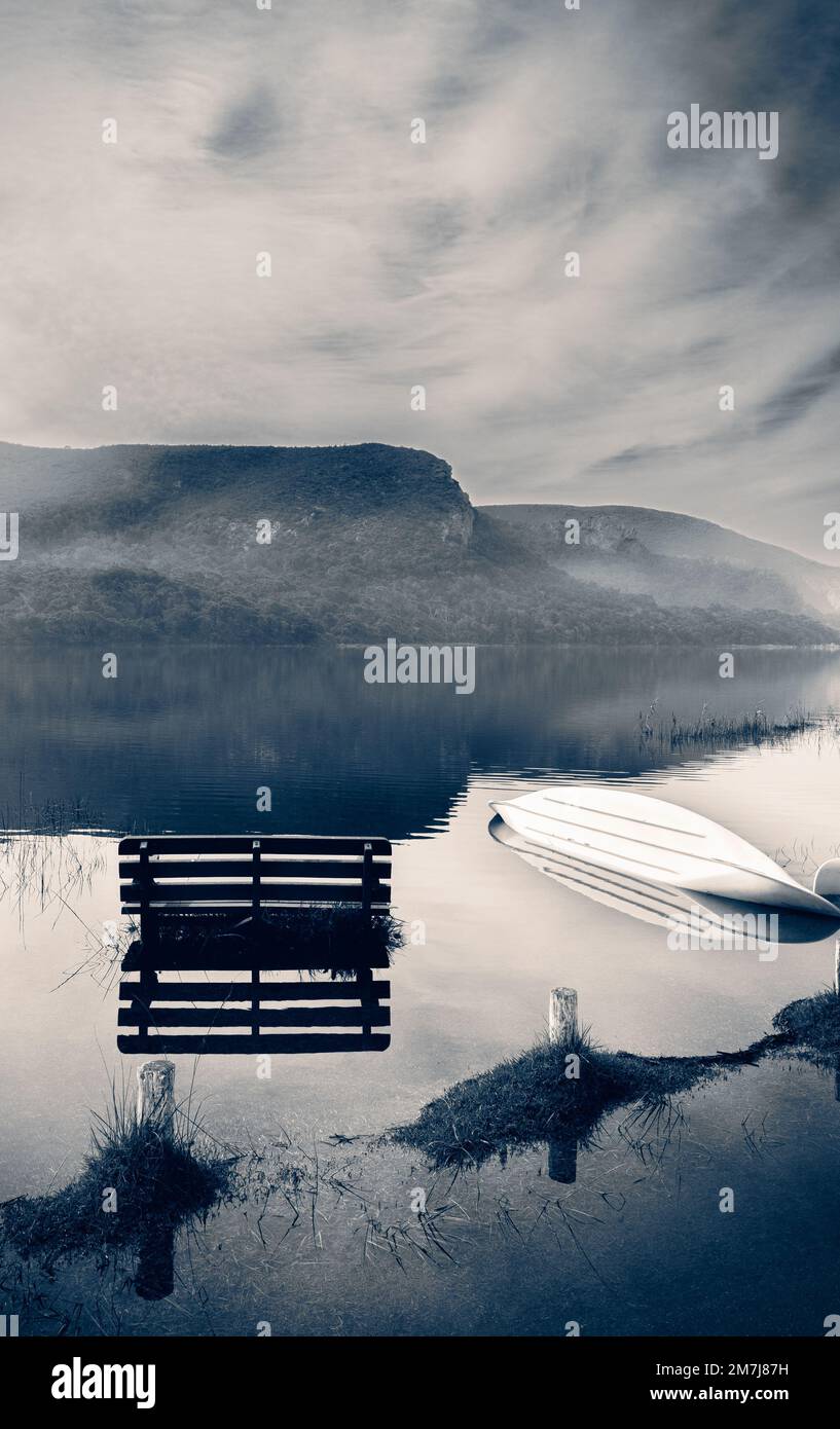 The calm lake water with inverted boat and mountains in the background ...