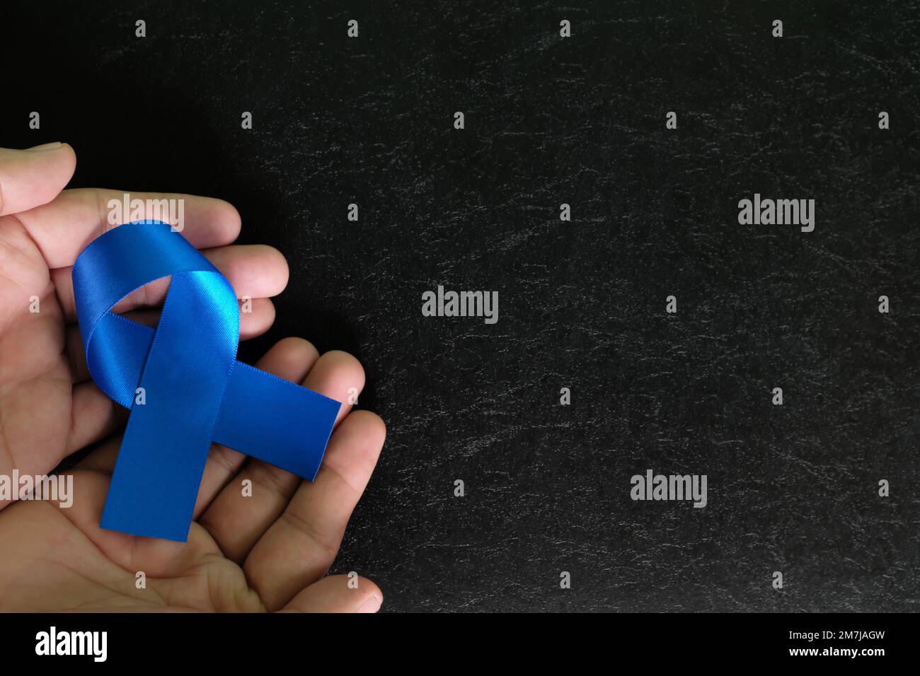 Human hand holding dark blue ribbon color on dark black background ...