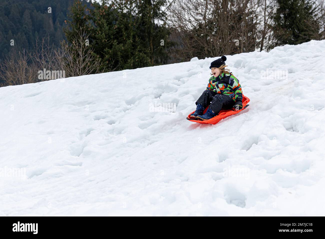 little caucasian girl bobsled down a snowy slope. Amused expression ...