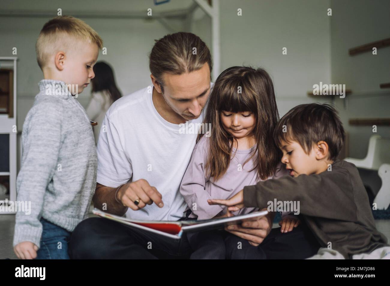Teacher reading story book with students in child care center Stock ...