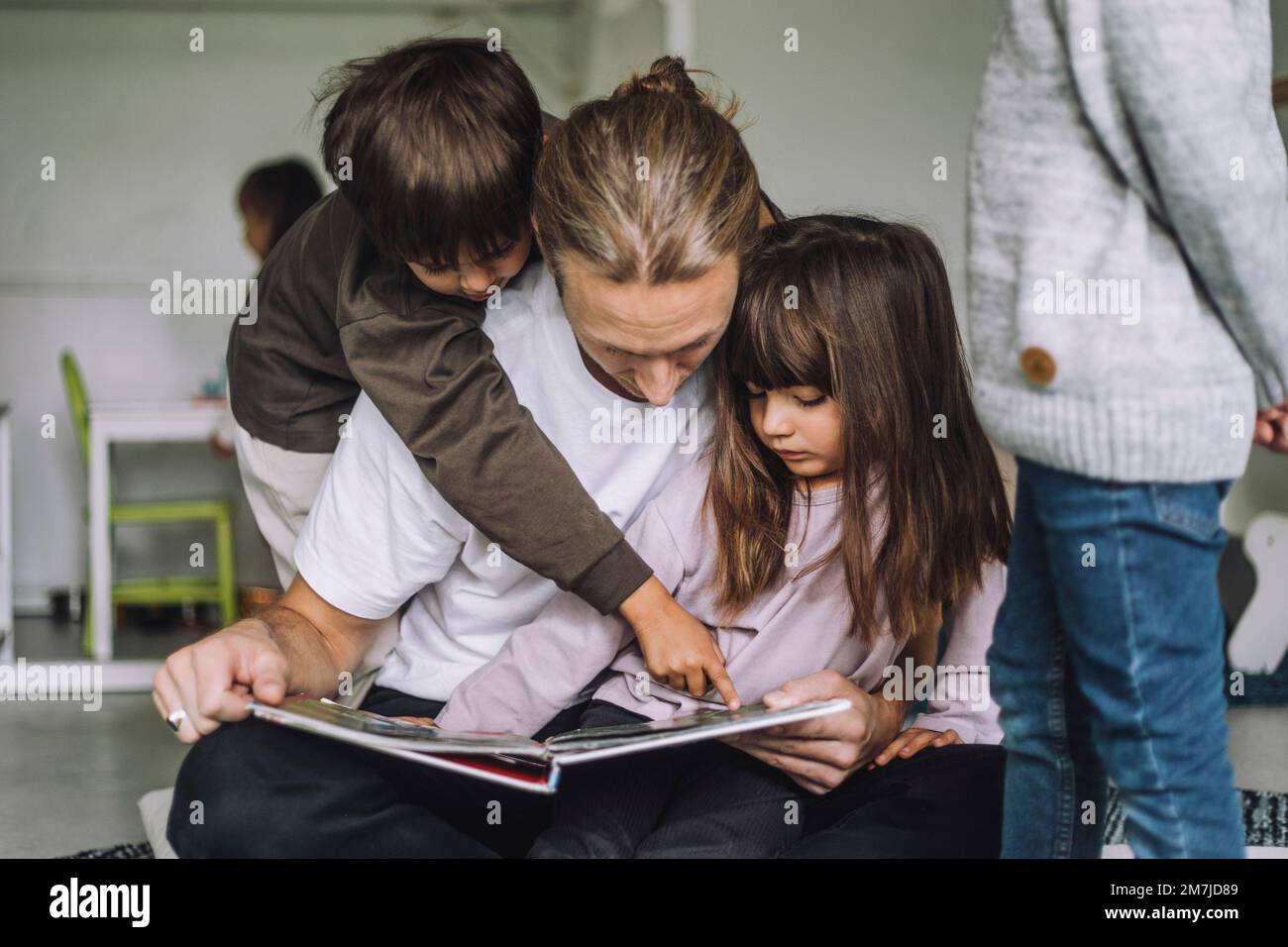 Boy pointing at picture book while male teacher telling story to him at ...