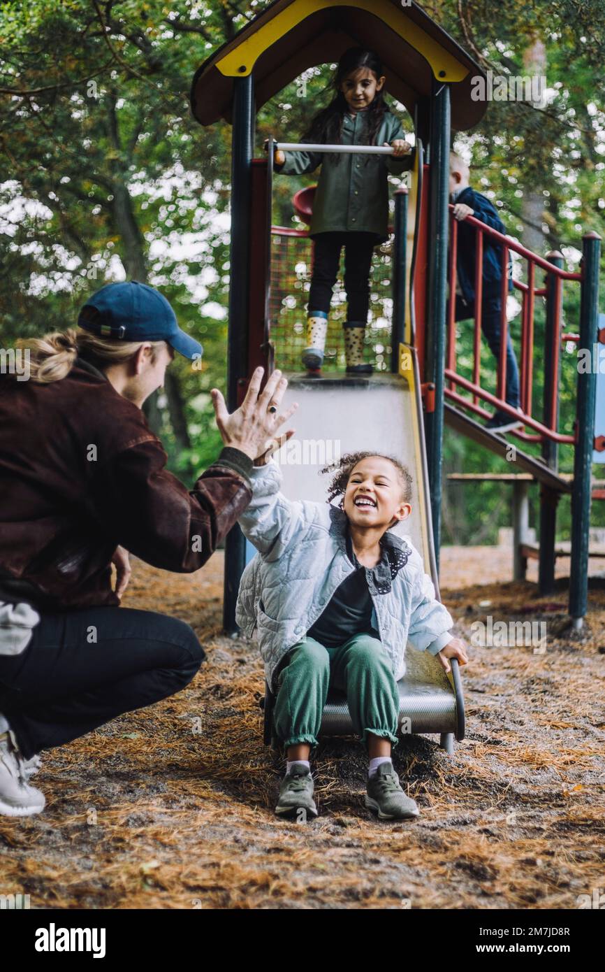 Cheerful girl giving high-five to male teacher while playing on slide ... Cheerful girl giving high-five to male teacher while playing on slide ...