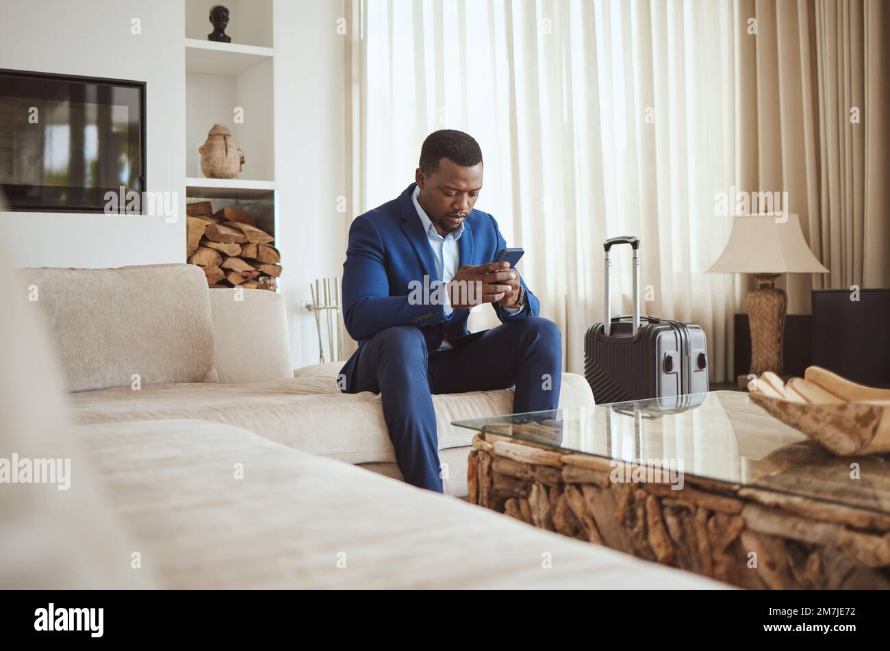 African businessman on phone in hotel room, reading email on smartphone ...