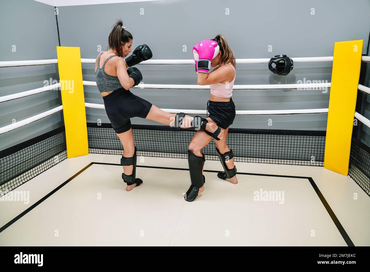Female kickboxer throwing a low kick to her colleague both wearing leg ...