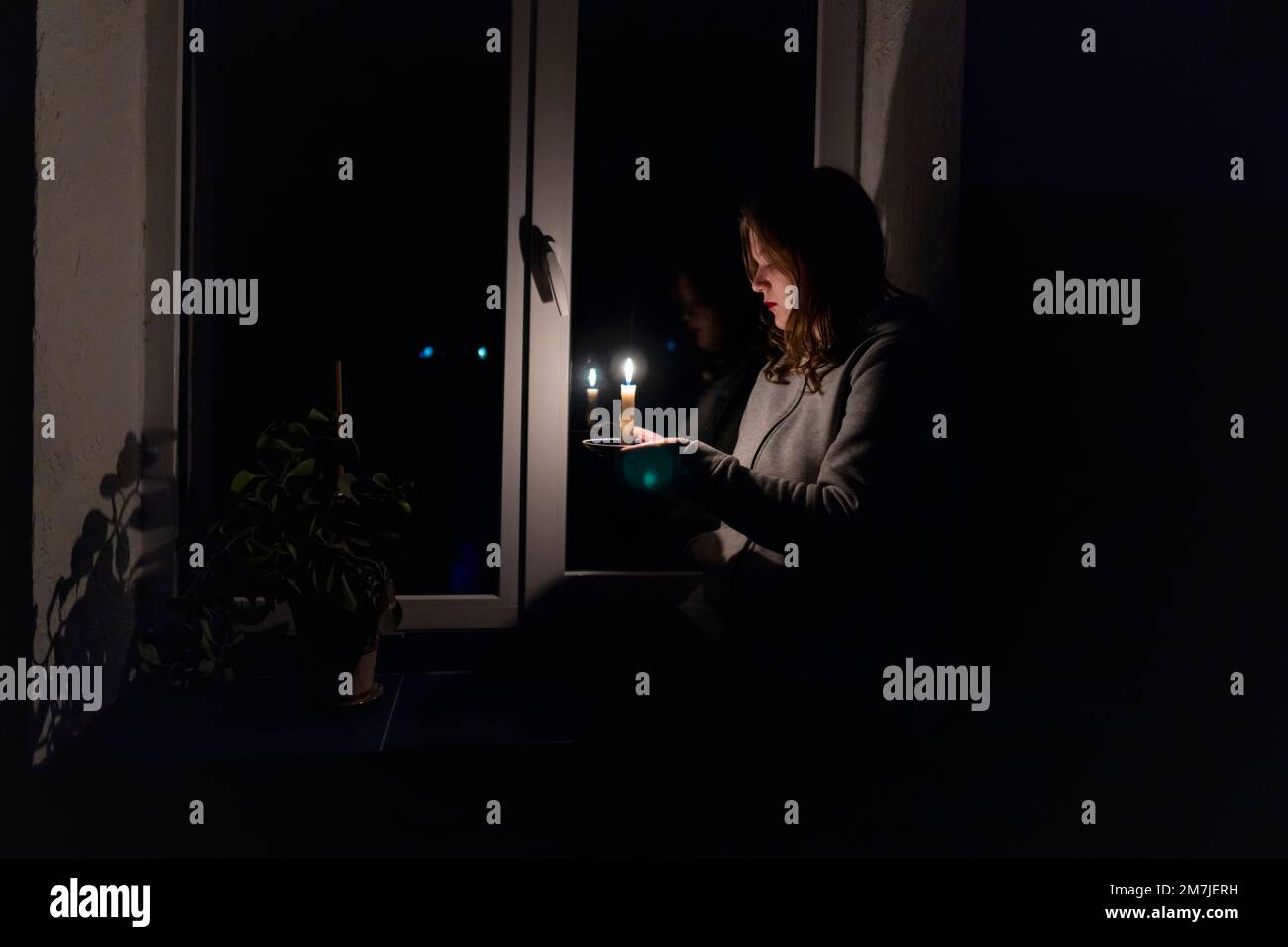 Girl with a burning candle in a dark room sits near the window ...