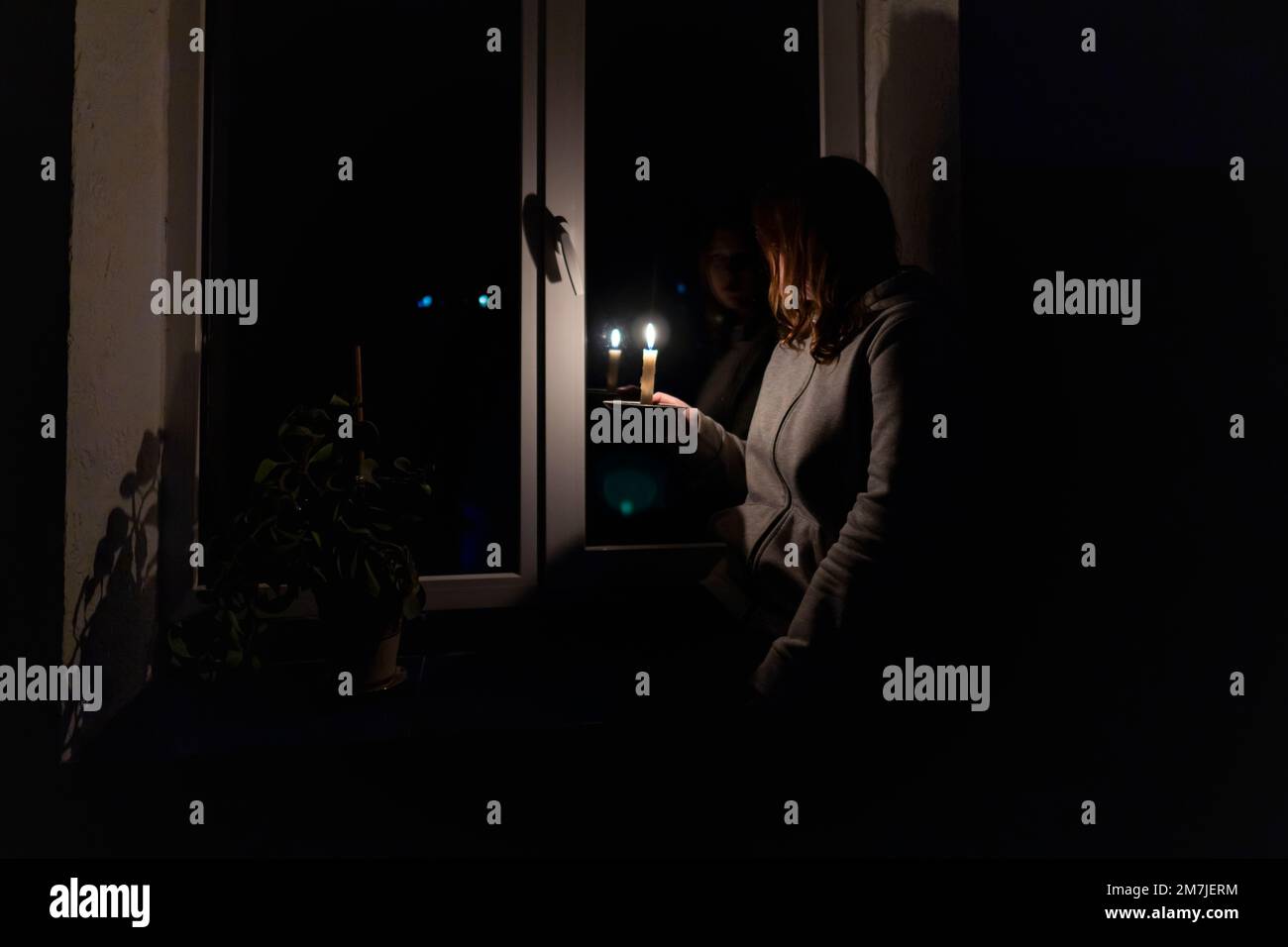 A girl with a burning candle in a dark room looks out the window ...