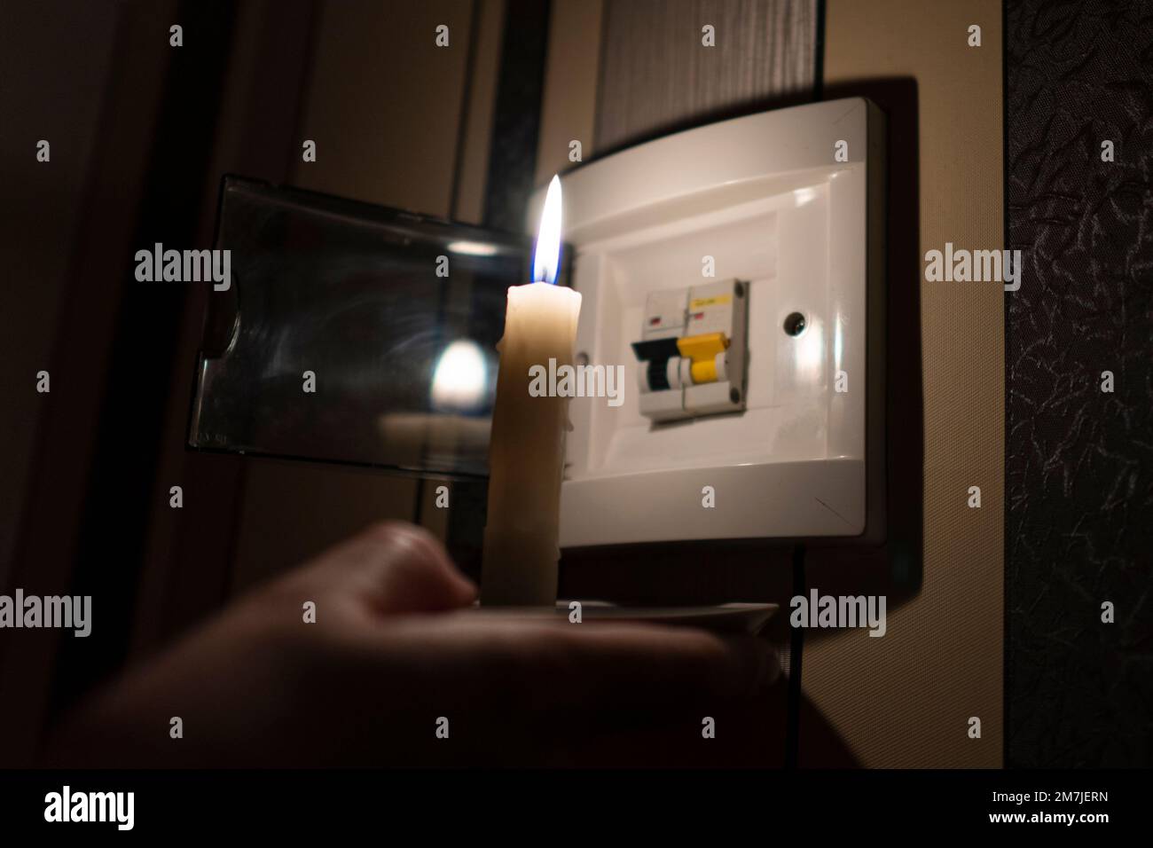 Hand with a burning candle illuminates an electrical switchboard (close ...
