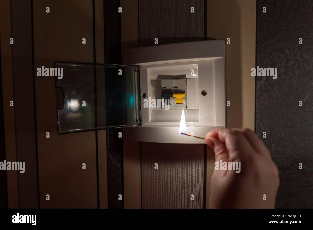 Hand with a burning match illuminates an electrical switchboard (close ...