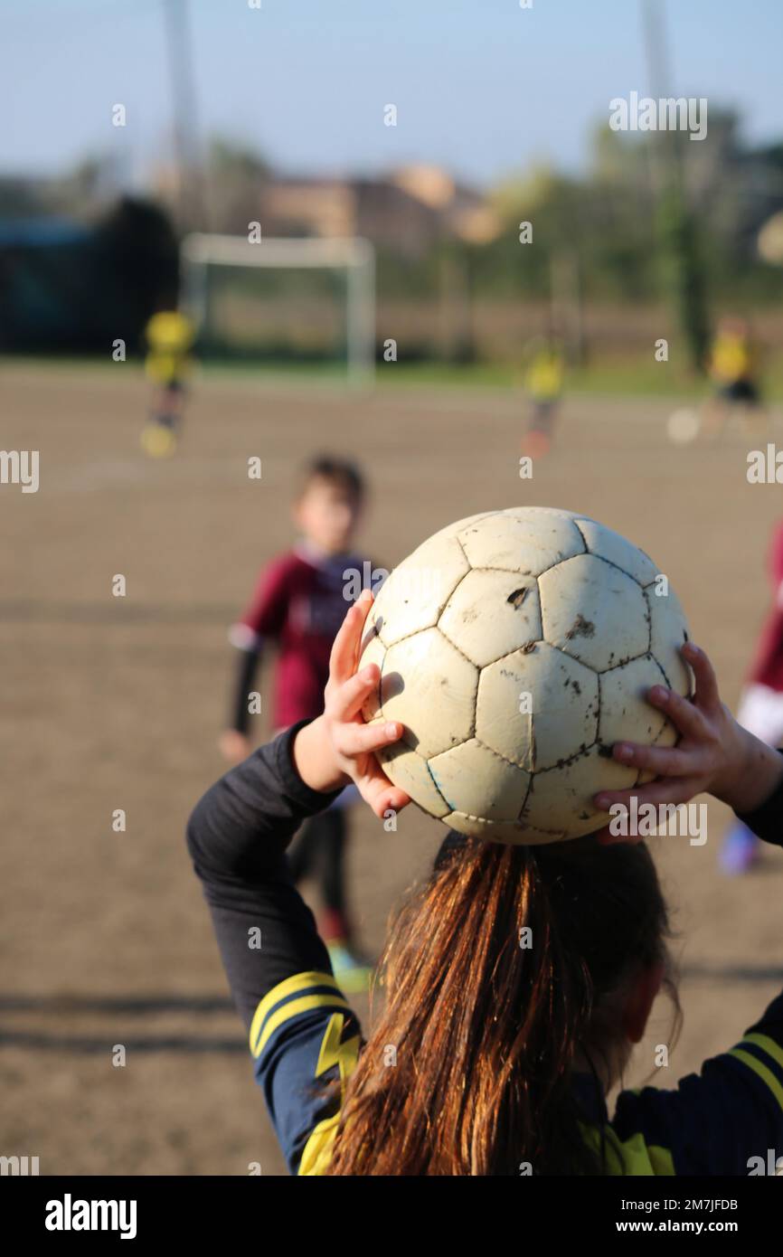 kicking a ball on a clay field with boys playing in the background ...