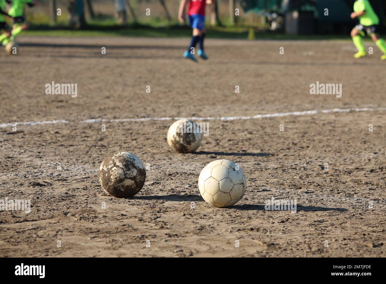 kicking a ball on a clay field with boys playing in the background ...