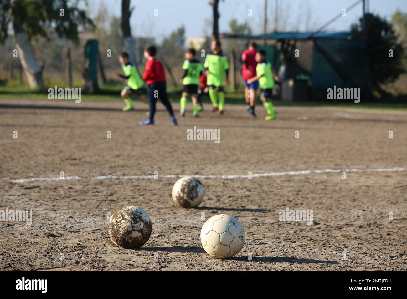 kicking a ball on a clay field with boys playing in the background ...