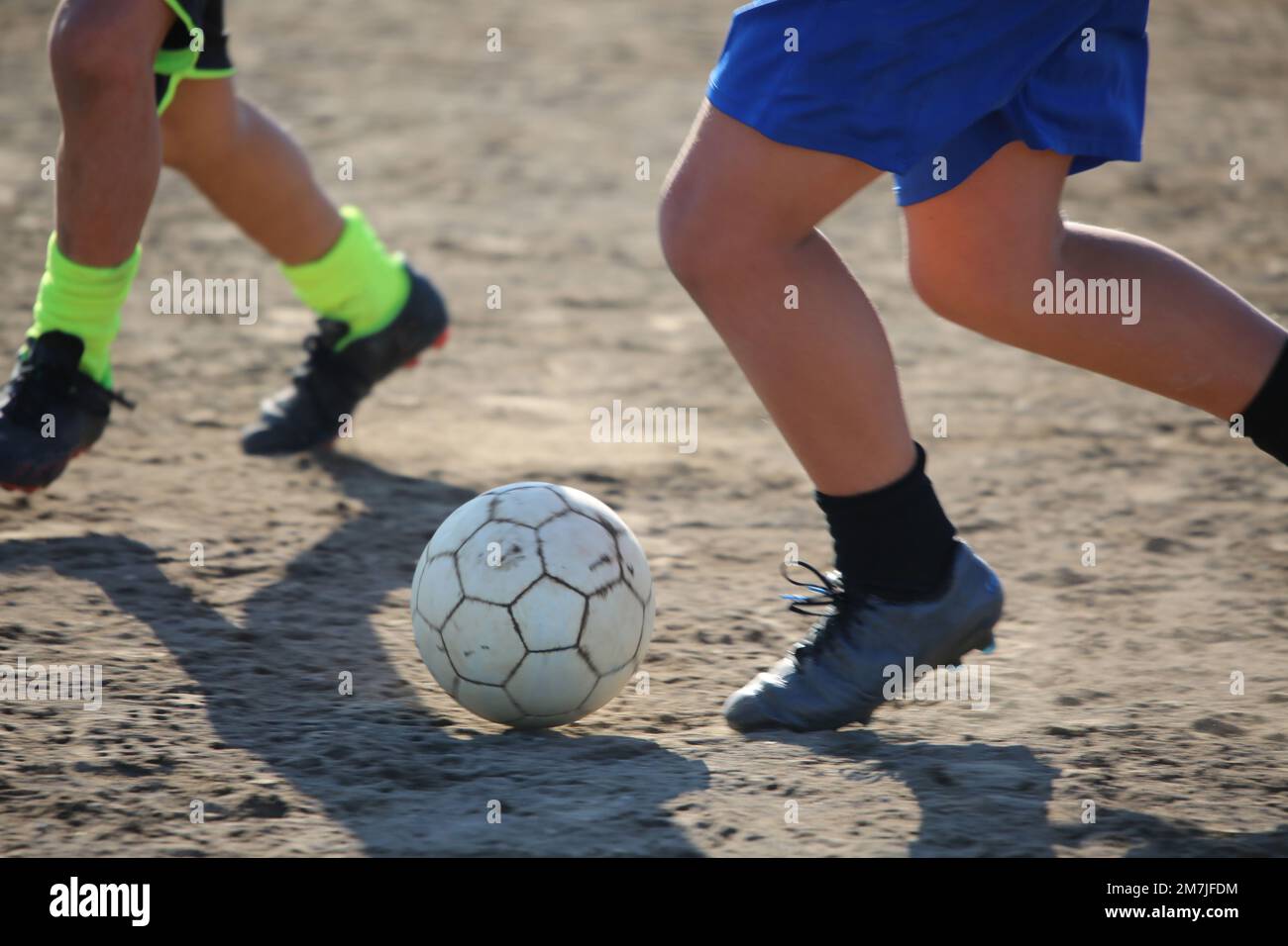 kicking a ball on a clay field with boys playing in the background ...