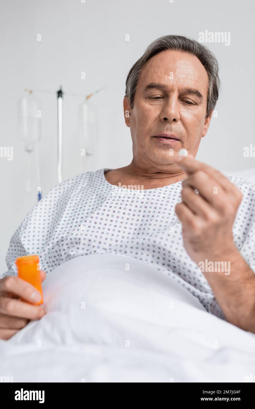 Grey Haired Patient Holding Pill While Sitting On Hospital Bed Stock