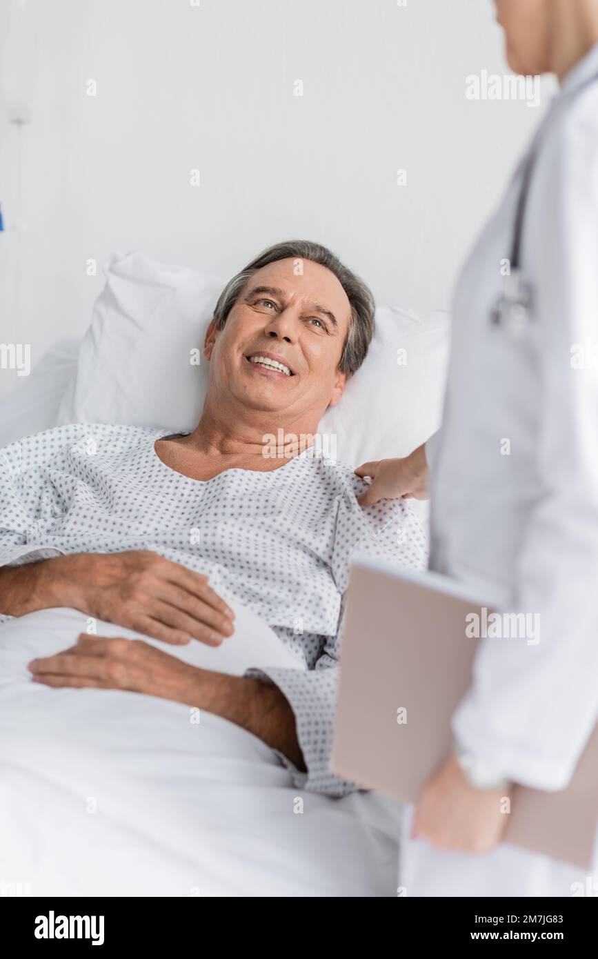 Blurred doctor with paper folder calming elderly patient in hospital ...