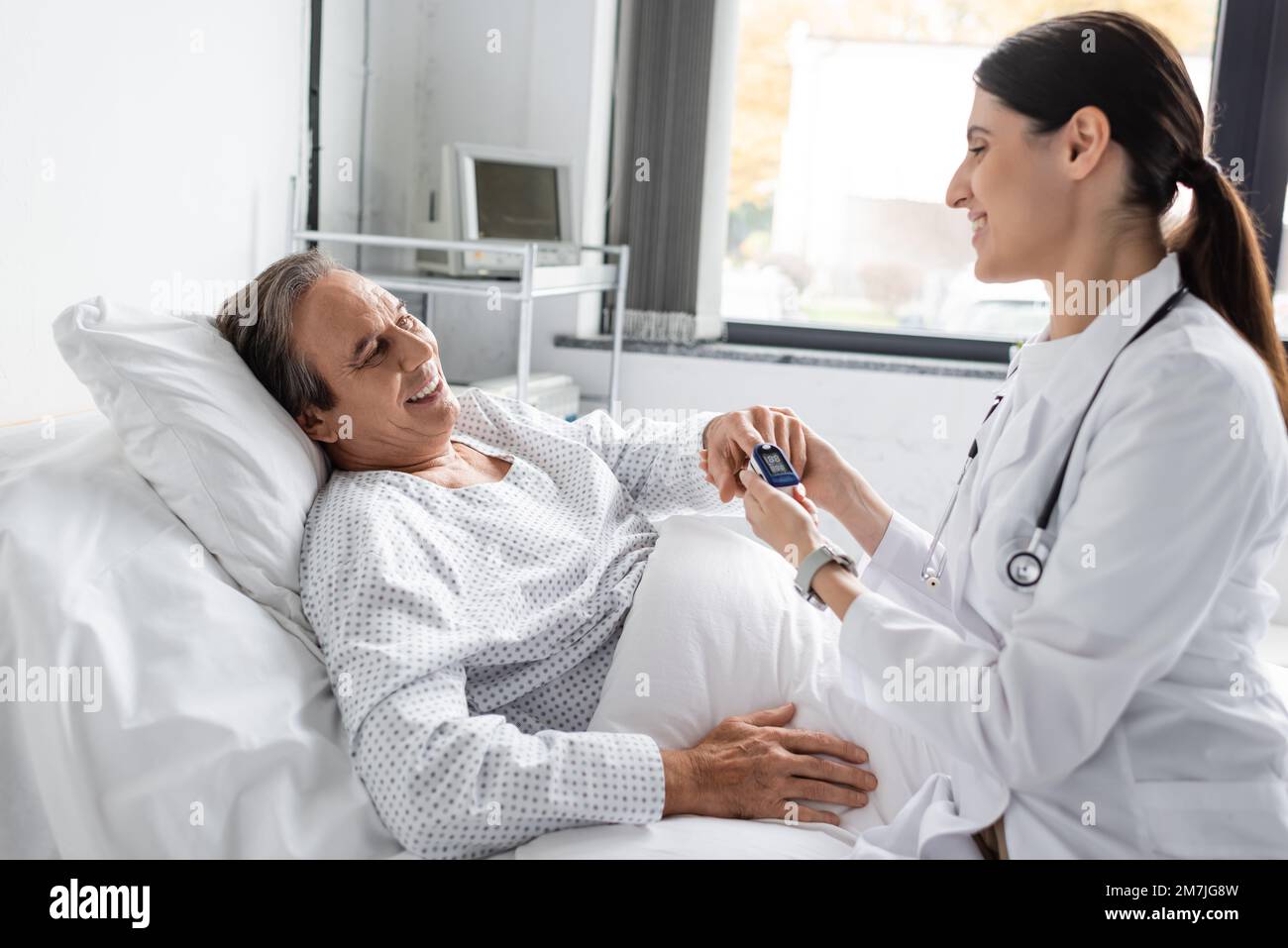 Positive doctor wearing pulse oximeter on finger of senior patient in ...