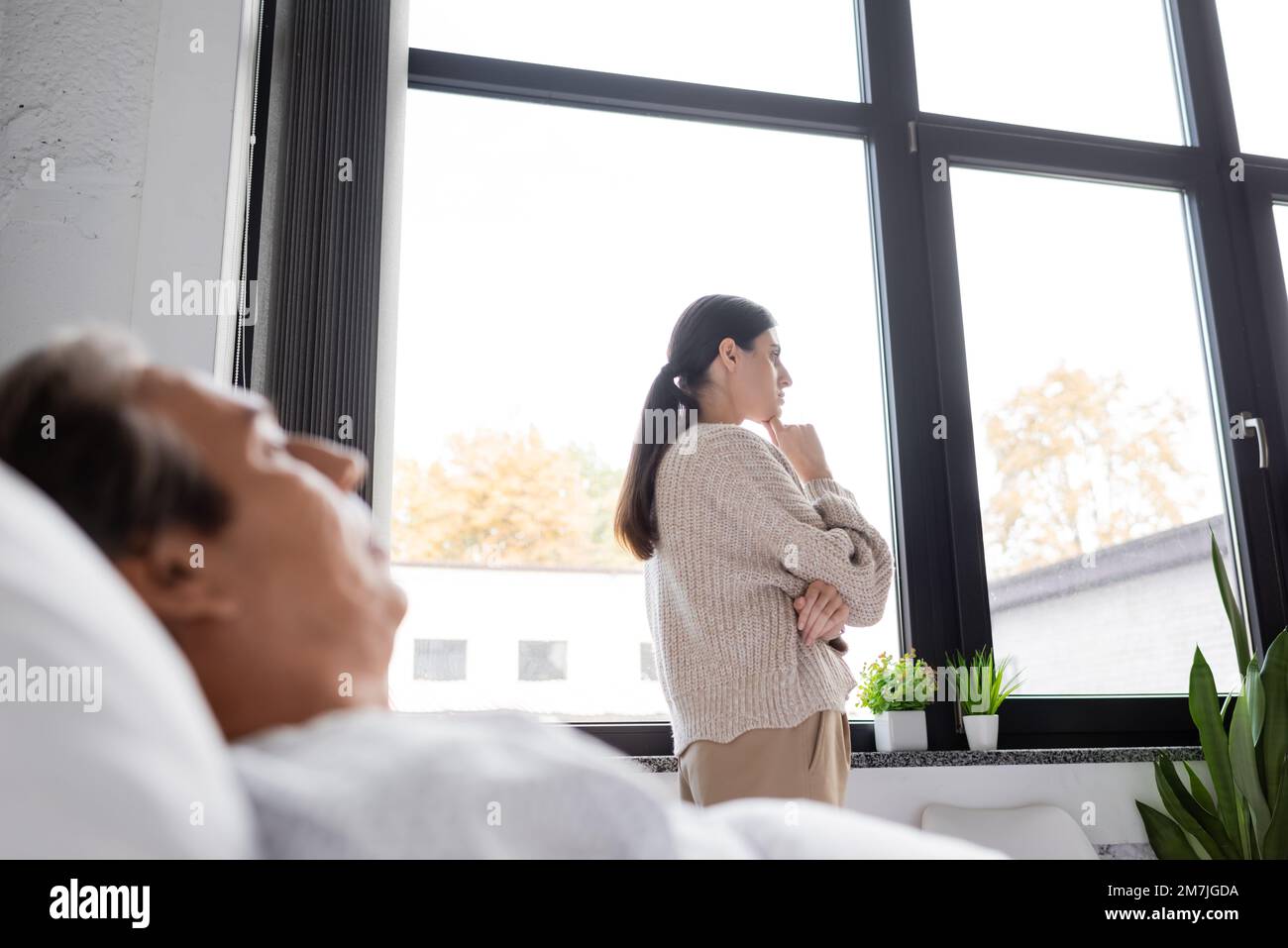 Side view of upset woman standing near blurred sick dad in hospital ...