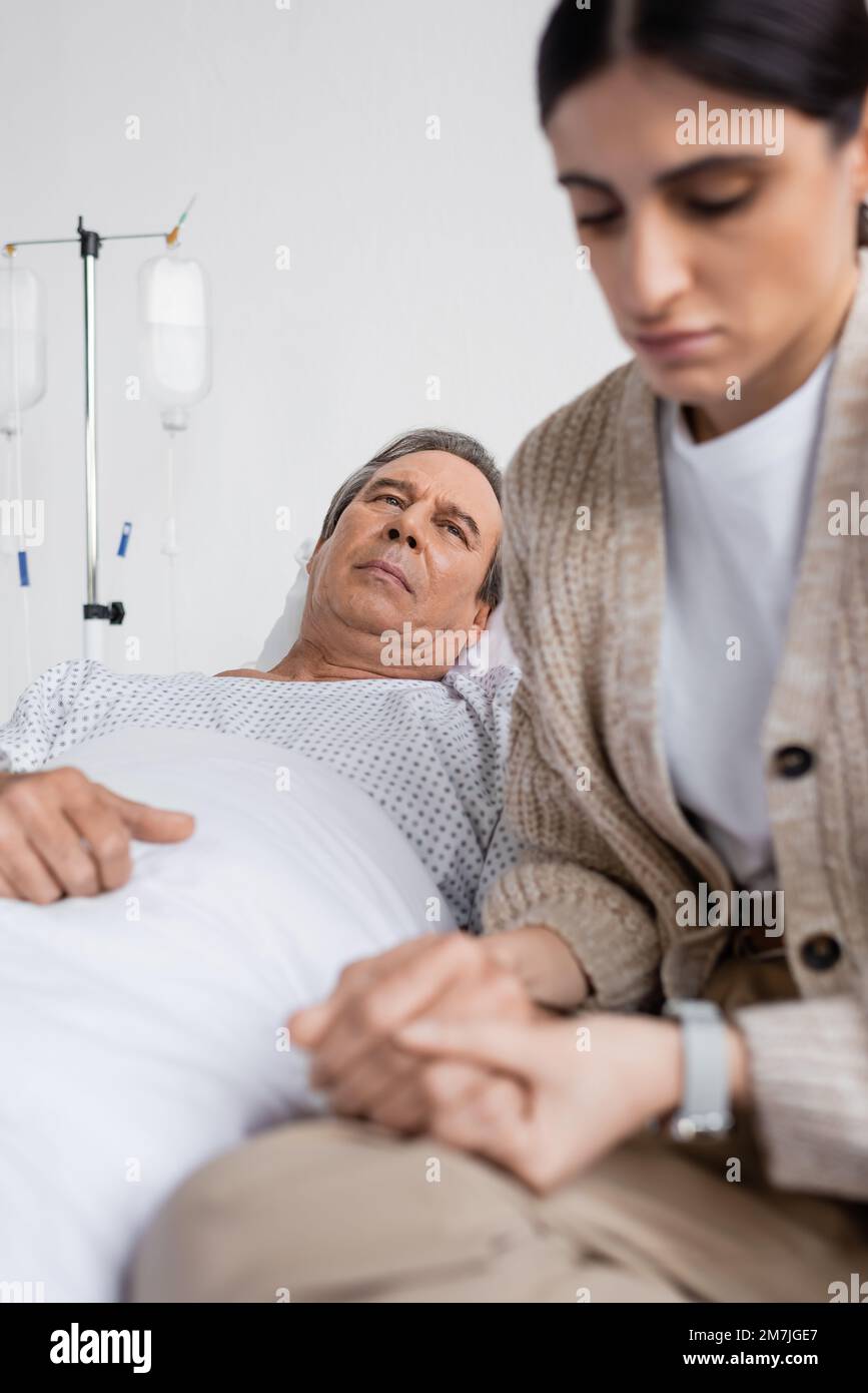Sick man looking at blurred upset daughter while lying on bed in ...
