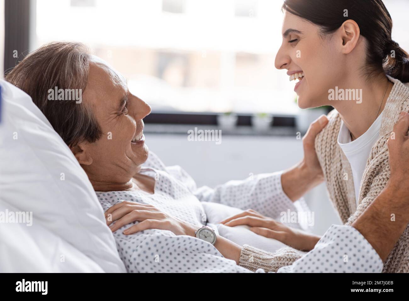 Side view of cheerful woman hugging father in patient gown in hospital ...