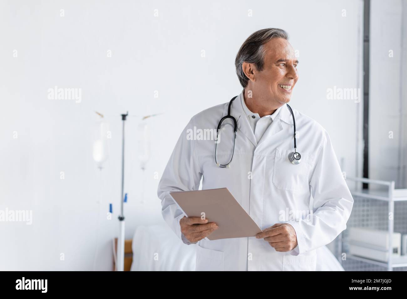 Elderly doctor holding paper folder and smiling in hospital ward,stock ...