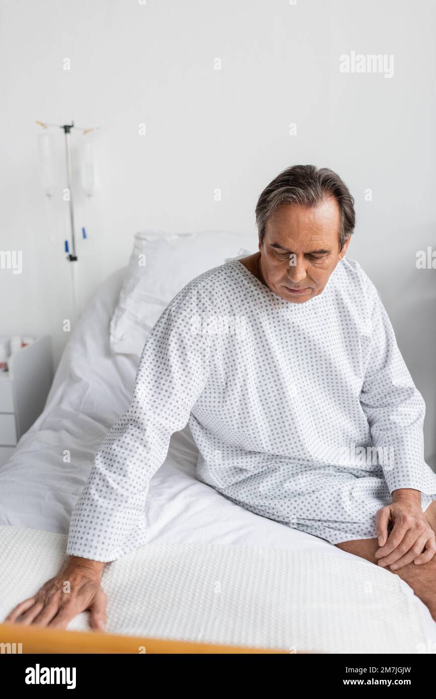 Upset senior patient in gown sitting on hospital bed,stock image Stock ...