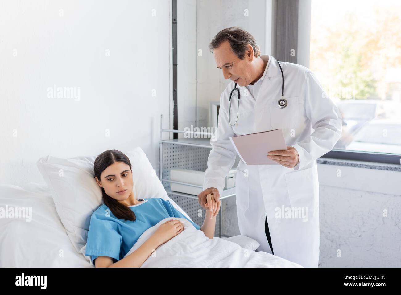 Senior doctor with paper folder holding hand of brunette patient in ...