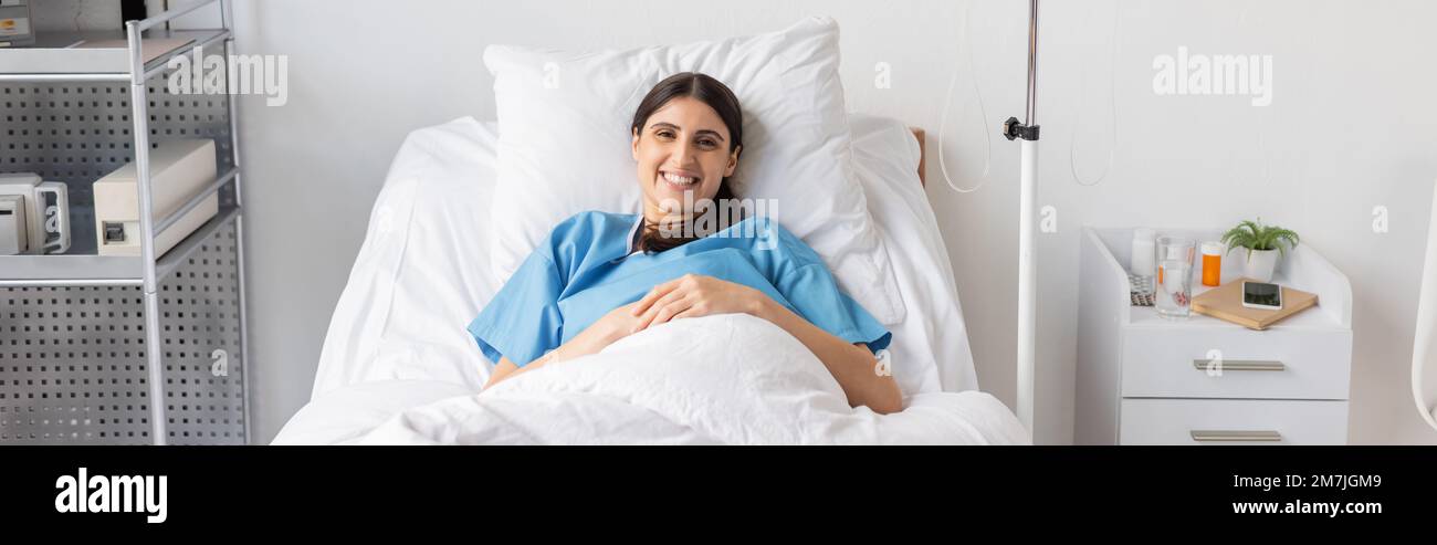 Positive patient smiling at camera on bed in hospital ward, banner ...