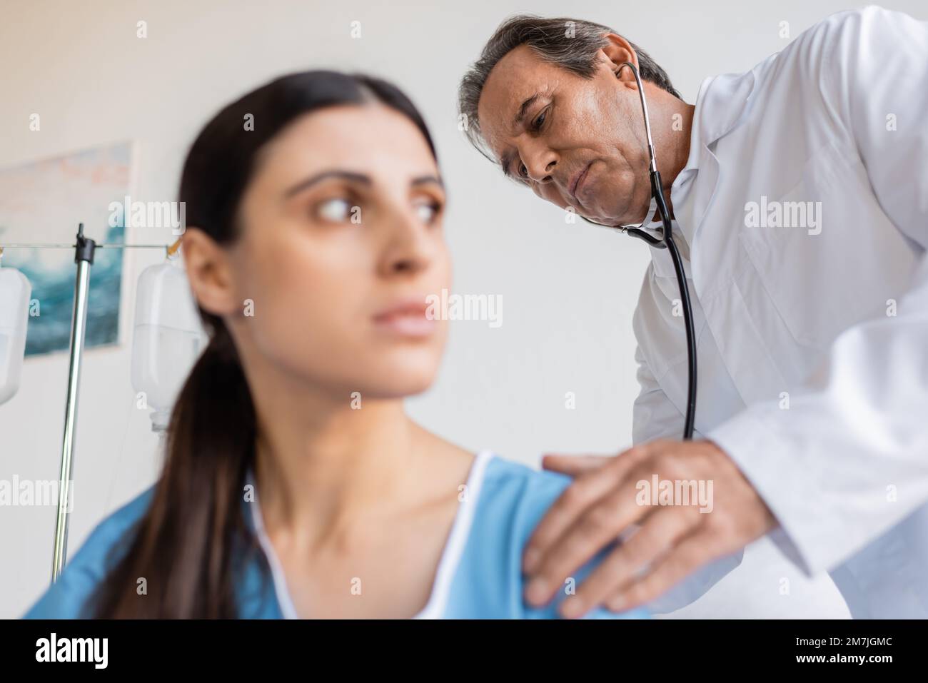 Senior doctor with stethoscope checking back of blurred patient in ...
