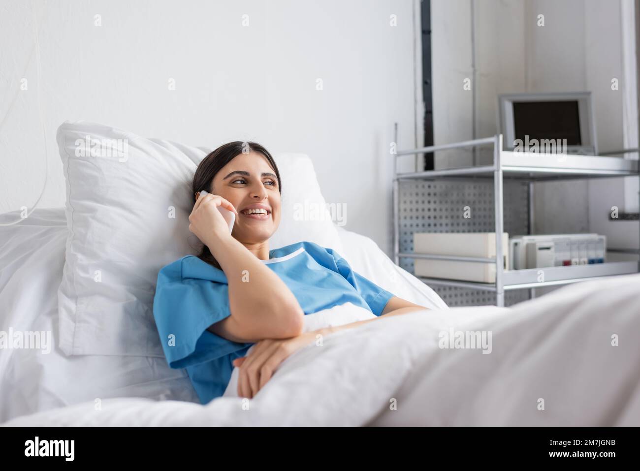 Positive patient talking on smartphone while lying on bed in clinic ...
